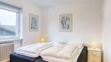 Quarto com cama, duas mesinhas de cabeceira, uma janela e duas obras de arte na parede.