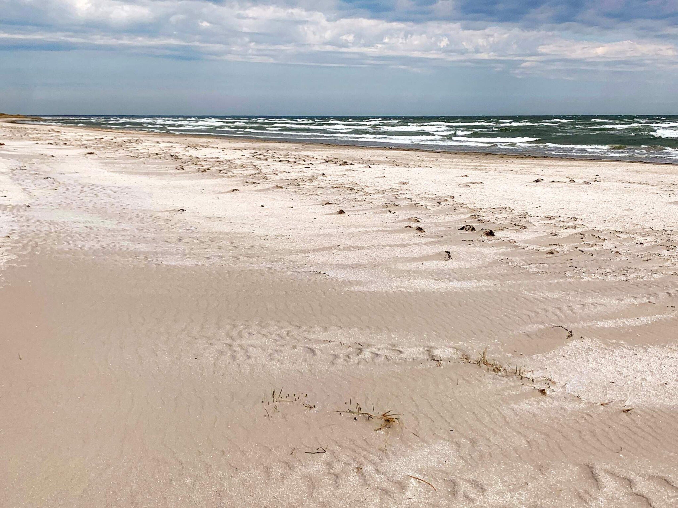 Uma praia com extensa faixa de areia e ondas do mar ao fundo.