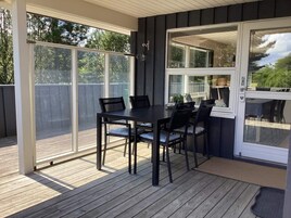 Varanda com mesa e cadeiras, porta de correr e vista para árvores.