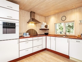 Uma cozinha moderna com armários de madeira, forno embutido, micro-ondas e janela com vista para o verde.