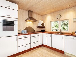 Cozinha moderna com armários de madeira, forno embutido e janela com vista para vegetação.