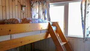 Uma cama beliche com escada de madeira, janela com cortinas e um radiador.