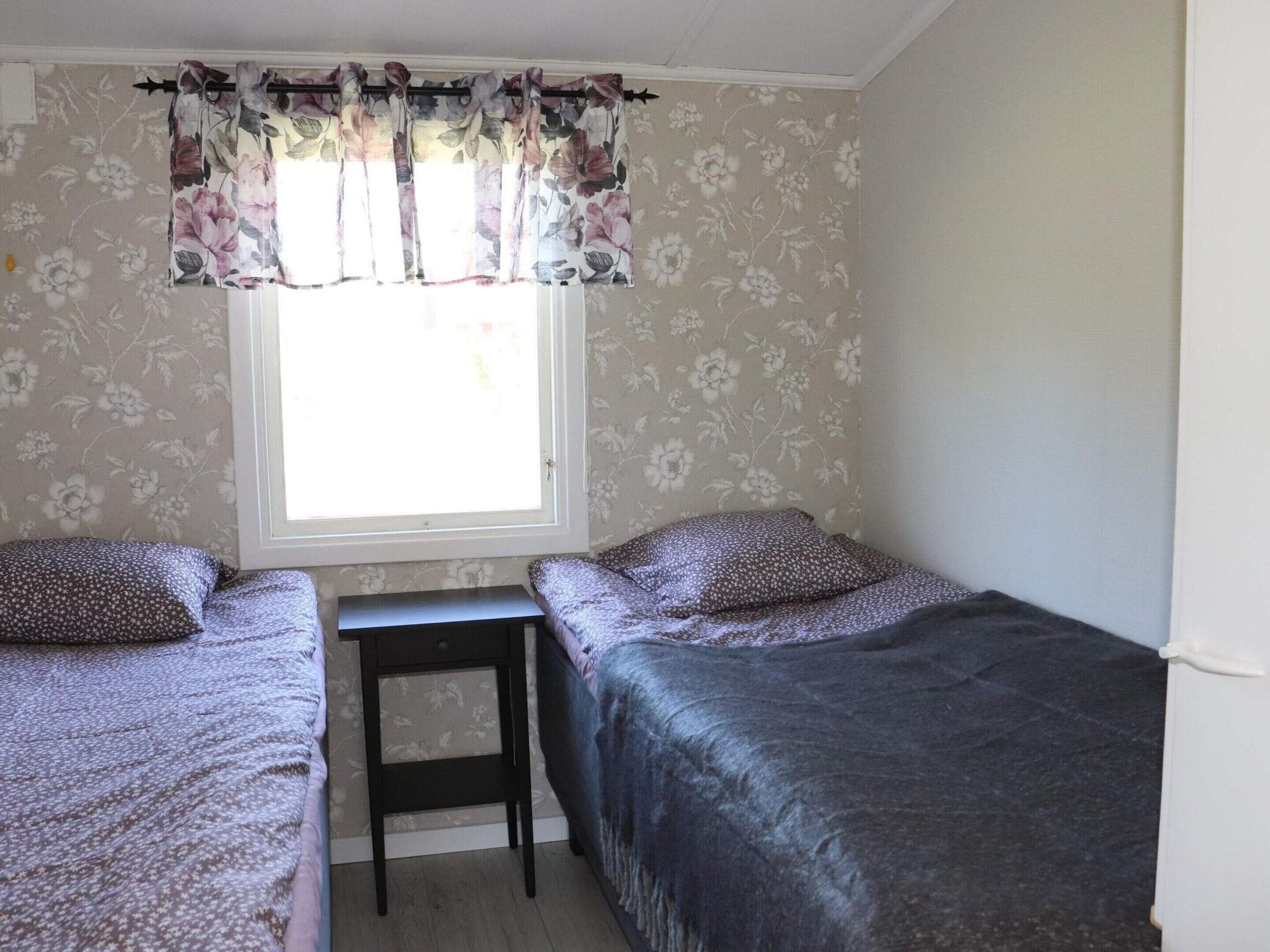 Quarto com duas camas de solteiro, uma mesa pequena e janela com cortinas florais.