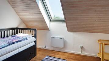 Quarto com teto inclinado, janela, cama, radiador e piso de madeira.