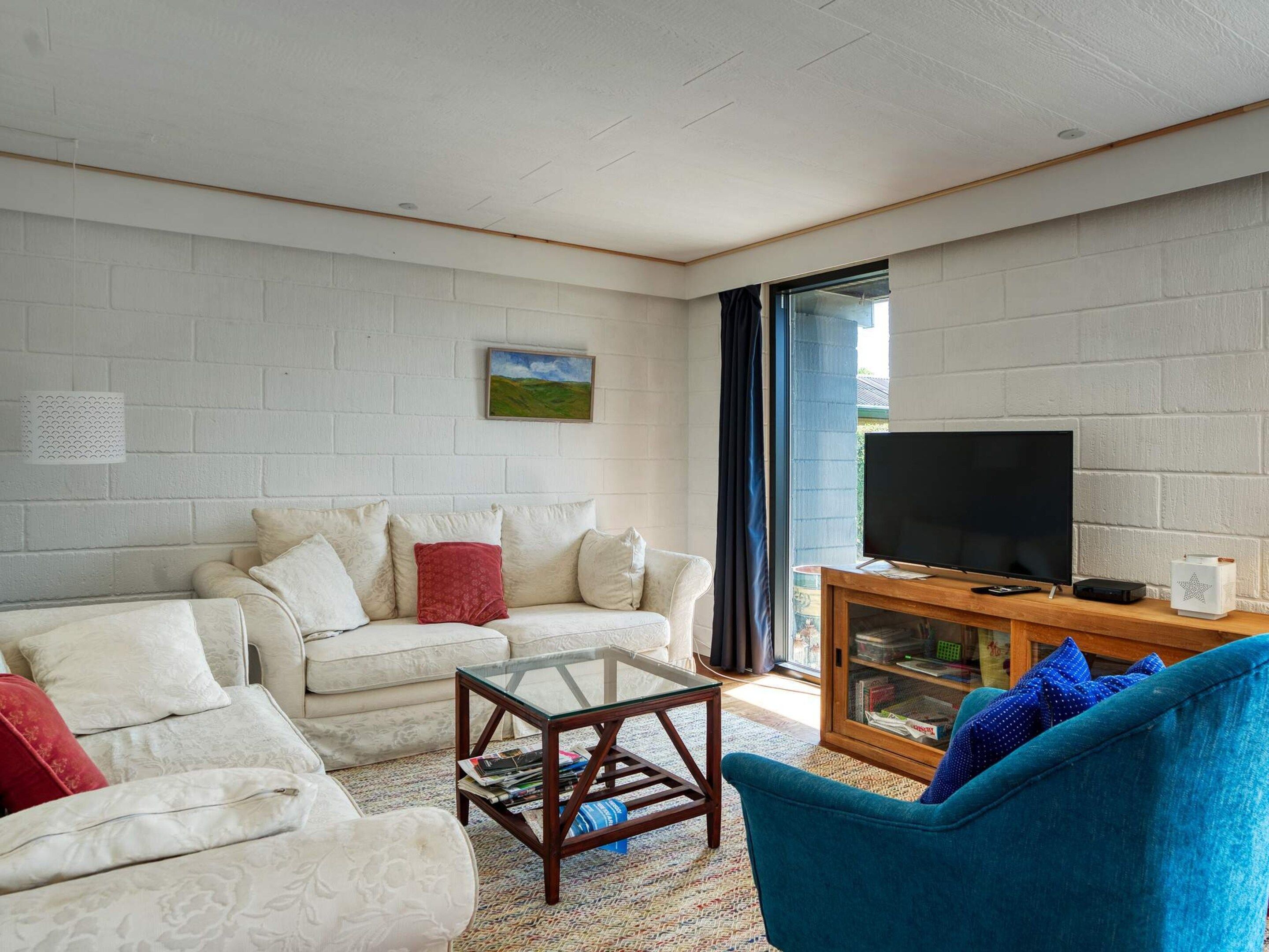 Sala de estar com sofá, mesa de centro, televisão sobre um suporte de madeira e janela com cortinas.