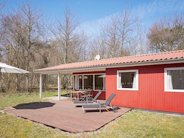 Um edifício vermelho com um alpendre, mobiliário exterior e vista para árvores sem folhas.