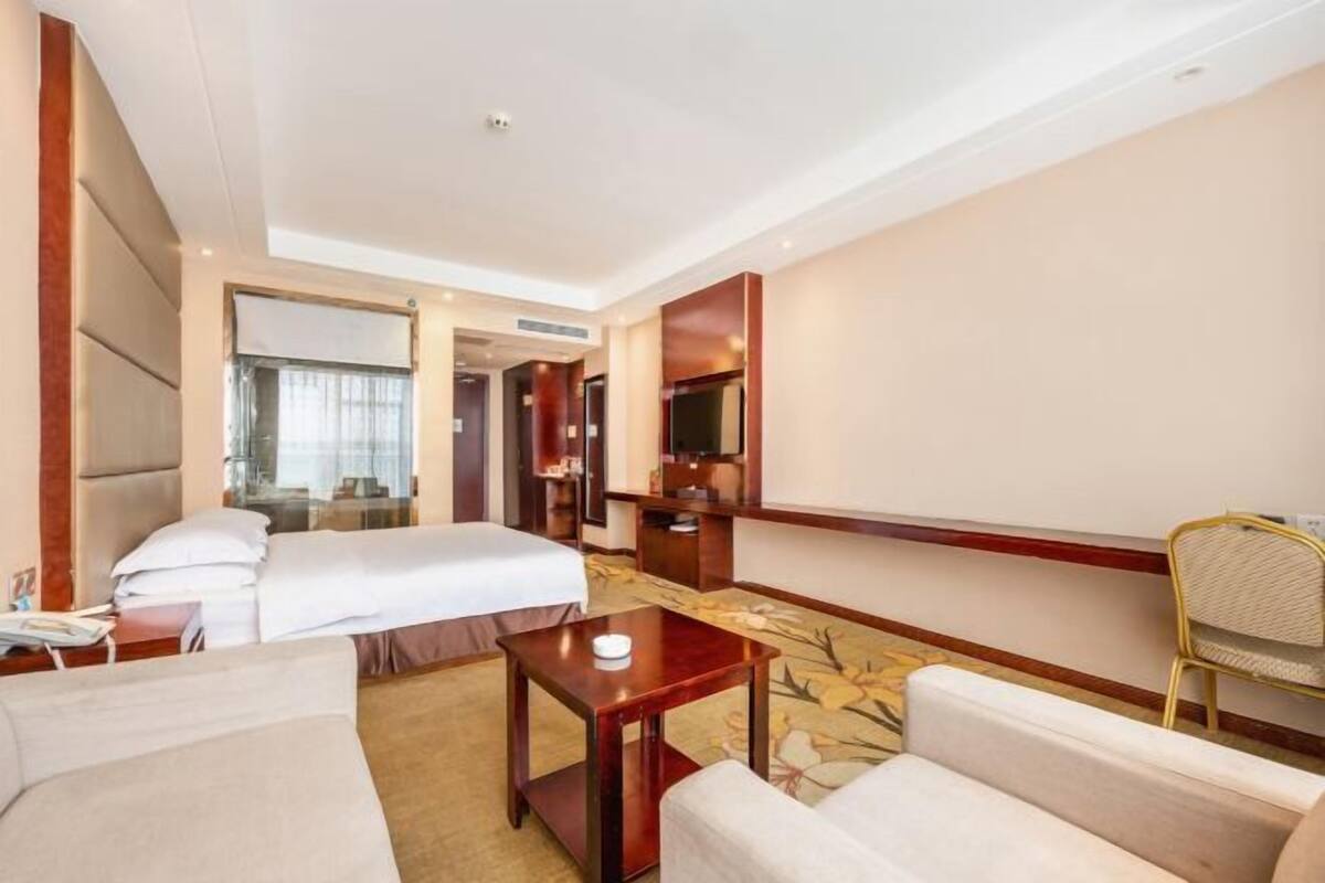 Quarto de hotel com duas camas, um sofá, uma mesinha, uma televisão e um espelho.