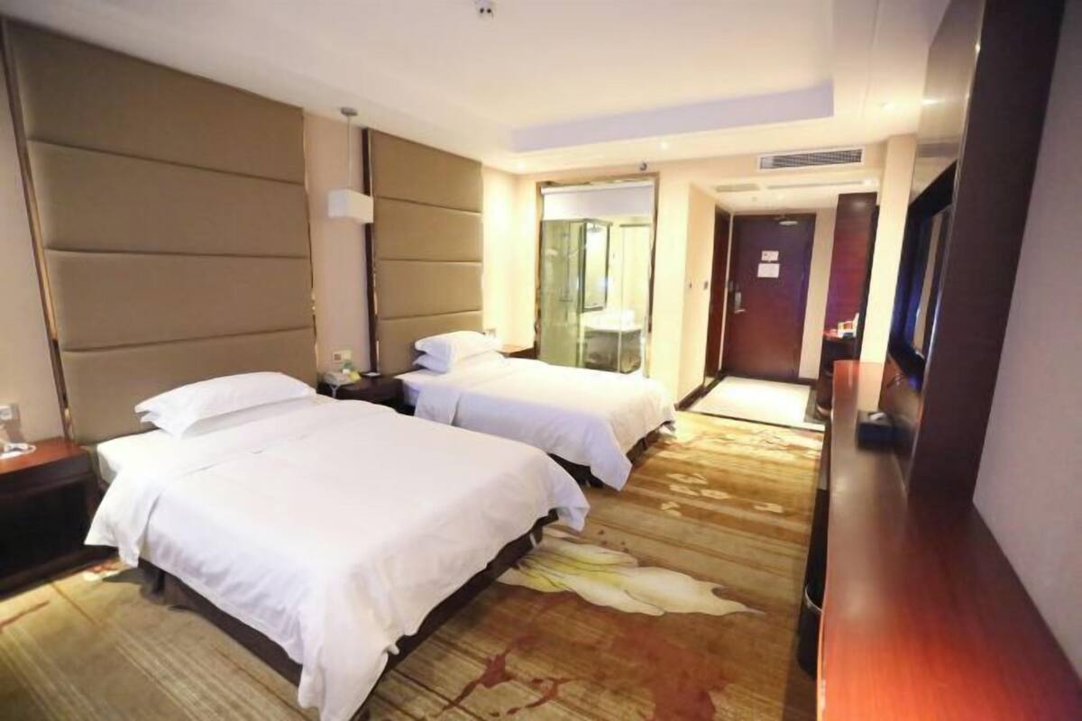 Quarto de hotel com duas camas, piso de madeira, um espelho grande e uma televisão.