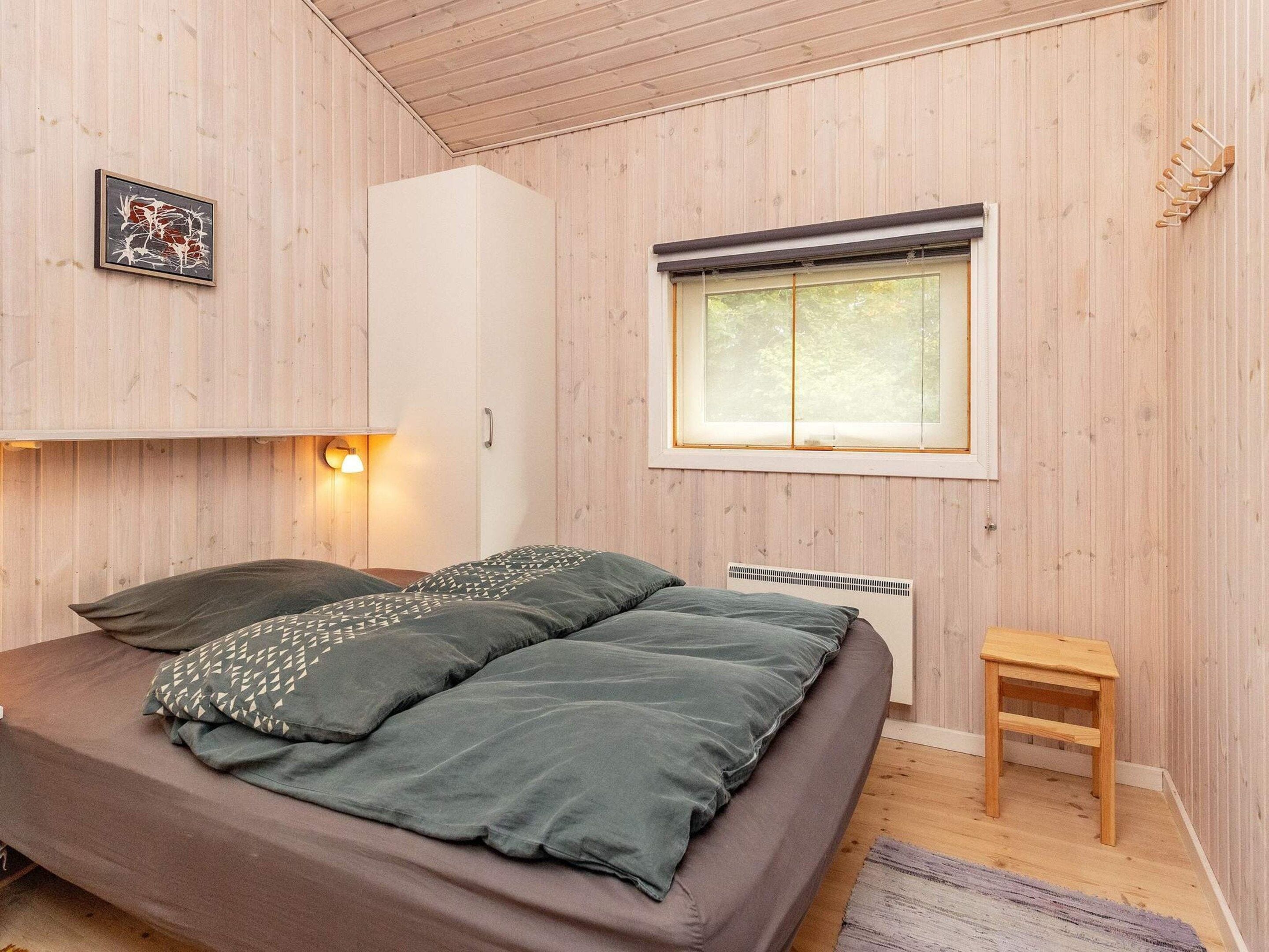 Quarto com cama, mesa de cabeceira, janela e um quadro na parede.