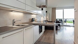 Cozinha moderna com ilha central, eletrodomésticos de aço inoxidável e vista para uma varanda.