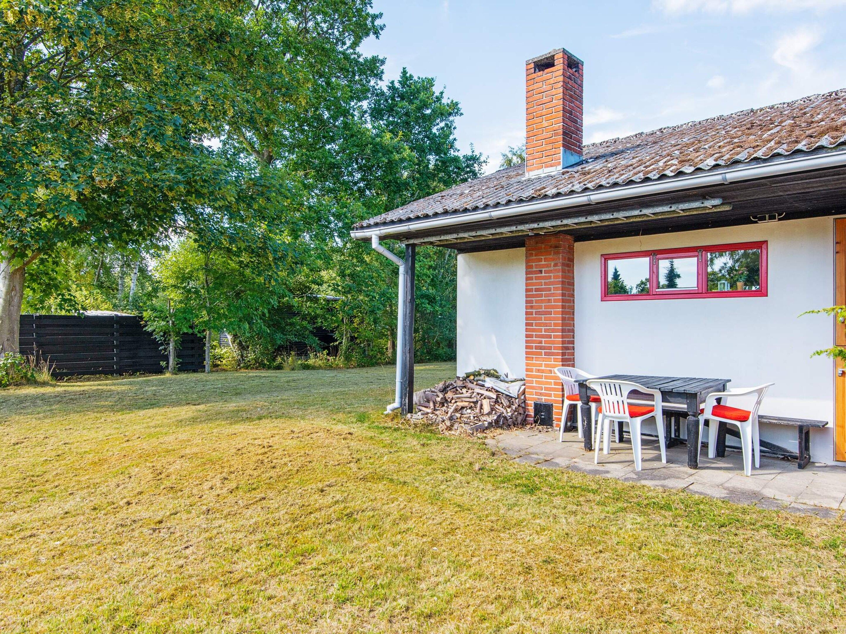 Uma casa com chaminé de tijolos, fachada branca e um pequeno pátio com mesa e cadeiras.