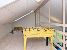 Quarto com mesa de futebol, piso de madeira e grandes janelas.