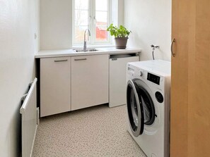 Cozinha compacta com máquina de lavar embutida, janela com planta e radiador.