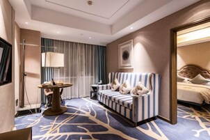 Quarto de hotel com sofá listrado, mesa redonda, cama com cabeceira estofada e um espelho grande.