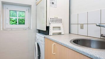 Uma cozinha compacta com máquina de lavar, um pequeno frigorífico, uma pia e uma janela com vista para o verde.