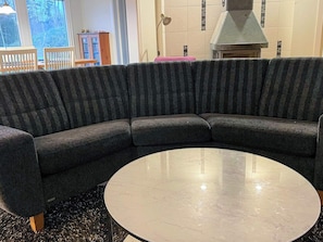 Um sofá modular com uma mesa de centro redonda de vidro numa sala com parede revestida em azulejos e lareira.