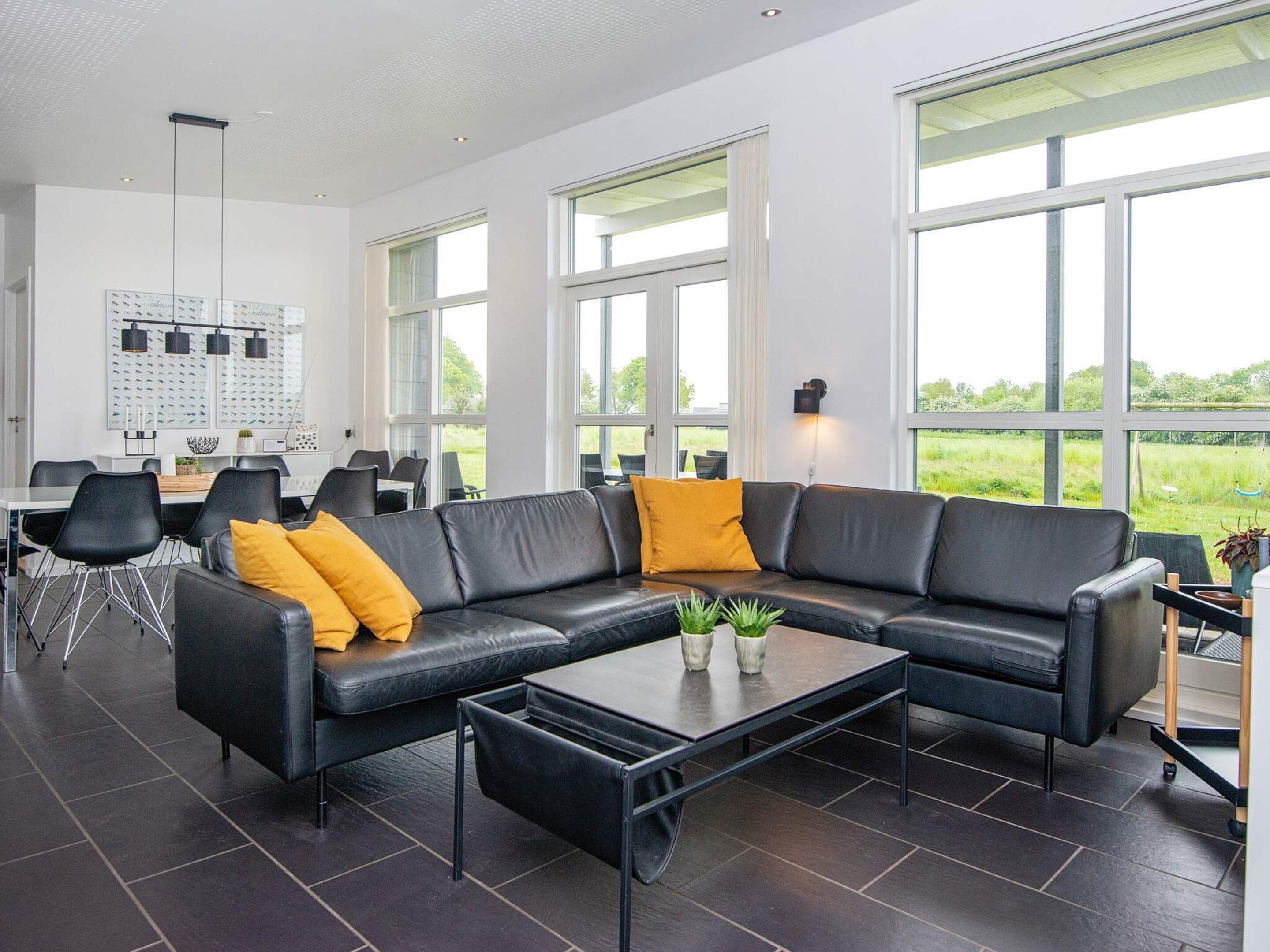 Uma sala de estar moderna com um sofá de couro preto, uma mesa de centro e janelas amplas com vista para o exterior.