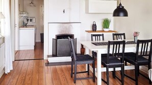 Uma área de refeições com mesa branca, cadeiras pretas, lareira e uma luminária pendente.