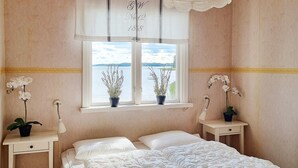 Quarto com cama, duas mesas de cabeceira, janela com vista e duas plantas em vasos.