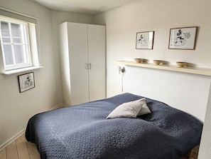 Quarto com cama, guarda-roupa, janela e prateleiras na parede com tigelas.