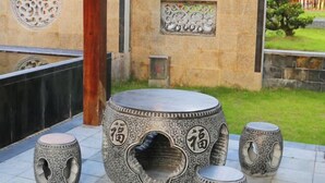 Um pátio com uma mesa de pedra e bancos, rodeado por paredes de pedra com esculturas decorativas.