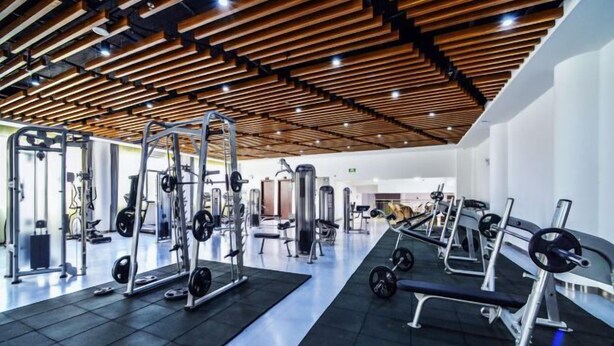 Uma academia com diversos equipamentos de musculação, piso de borracha preta e vigas de madeira no teto.
