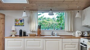 Cozinha compacta com janela, armários de madeira, chaleira, torradeira e pia.