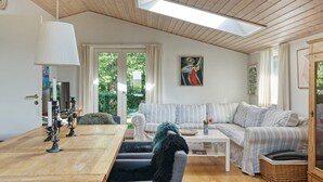 Uma sala de estar moderna com teto de madeira, uma mesa de jantar com velas, um conjunto de sofás e um quadro na parede.