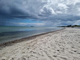 Uma praia com areal pedregoso, águas calmas e céu nublado.
