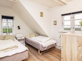 Quarto com teto inclinado, uma cama, mesa de cabeceira, cómoda e duas janelas.
