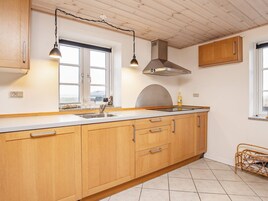 Cozinha com armários de madeira, pia de aço inoxidável, luminárias pendentes e janela com vista.