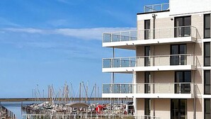 Um edifício com vários andares e varandas que dão para uma marina com barcos.