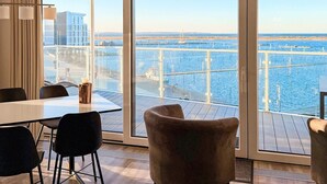Quarto de hotel moderno com uma grande janela que oferece vista para uma marina e para a água.