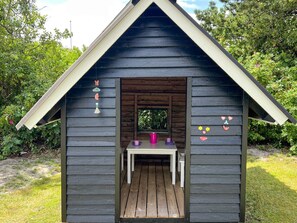 Uma casinha de madeira com telhado inclinado, uma mesa pequena e um banco.