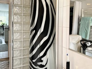 Casa de banho com espelho, porta-toalhas e cortina de chuveiro com padrão de zebra.