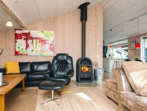 Uma sala de estar aconchegante com um sofá de couro preto, uma mesa de centro de madeira, uma poltrona de couro preto, uma mesa de centro com tampo de vidro e um sofá bege, além de uma lareira a lenha de madeira preta.