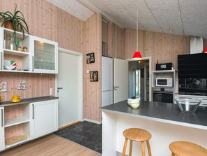 Uma cozinha moderna com paredes de painel de madeira, armários brancos, uma ilha central com banquetas e uma luminária pendente vermelha.
