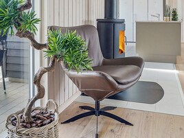 Uma sala de estar moderna com poltrona de couro marrom, piso de madeira, lareira e um vaso com planta.
