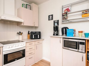 Uma cozinha moderna com fogão, forno, micro-ondas e cafeteira. Há armários, uma prateleira com livros e uma xícara de café no balcão.