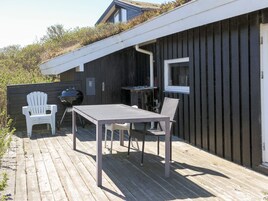 Um deck de madeira com mesa, cadeiras, churrasqueira e janela com vista para um jardim.