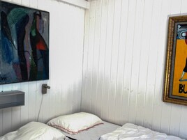 Um quarto com uma cama, uma parede branca, uma pintura e um quadro emoldurado.