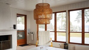 Uma sala de estar aconchegante com lareira, uma janela grande com vista para o exterior e uma luminária pendente de vime.