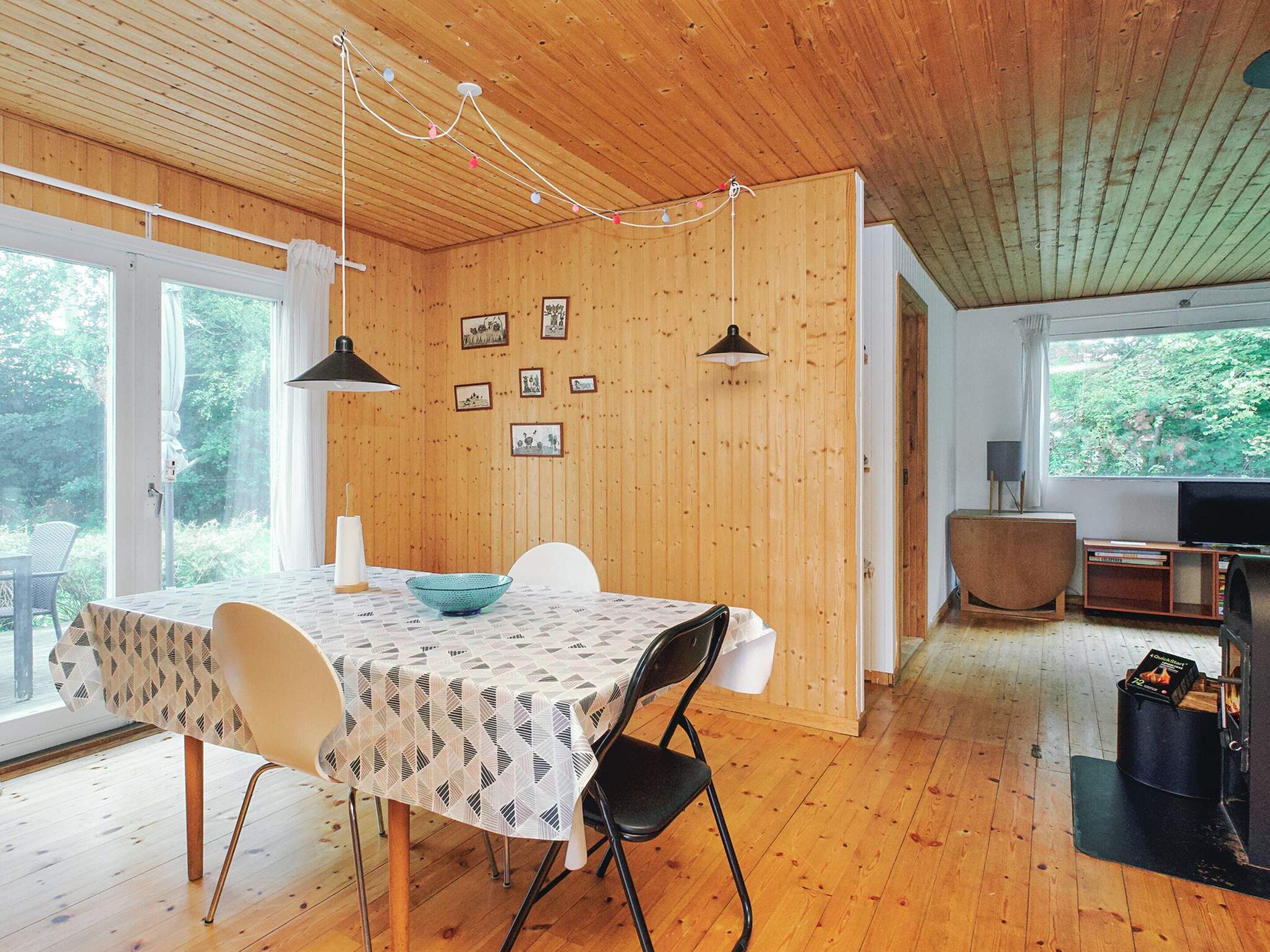 Interior em madeira com uma mesa de jantar, cadeiras, luminária pendente e quadros nas paredes.