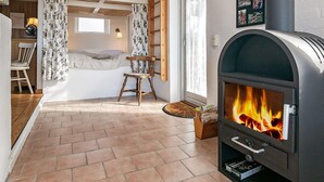 Um quarto aconchegante com cama, uma cadeira de madeira, lareira e uma janela com cortinas.