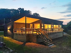 Uma casa moderna com fachada envidraçada, deck de madeira e escadaria que leva à entrada.