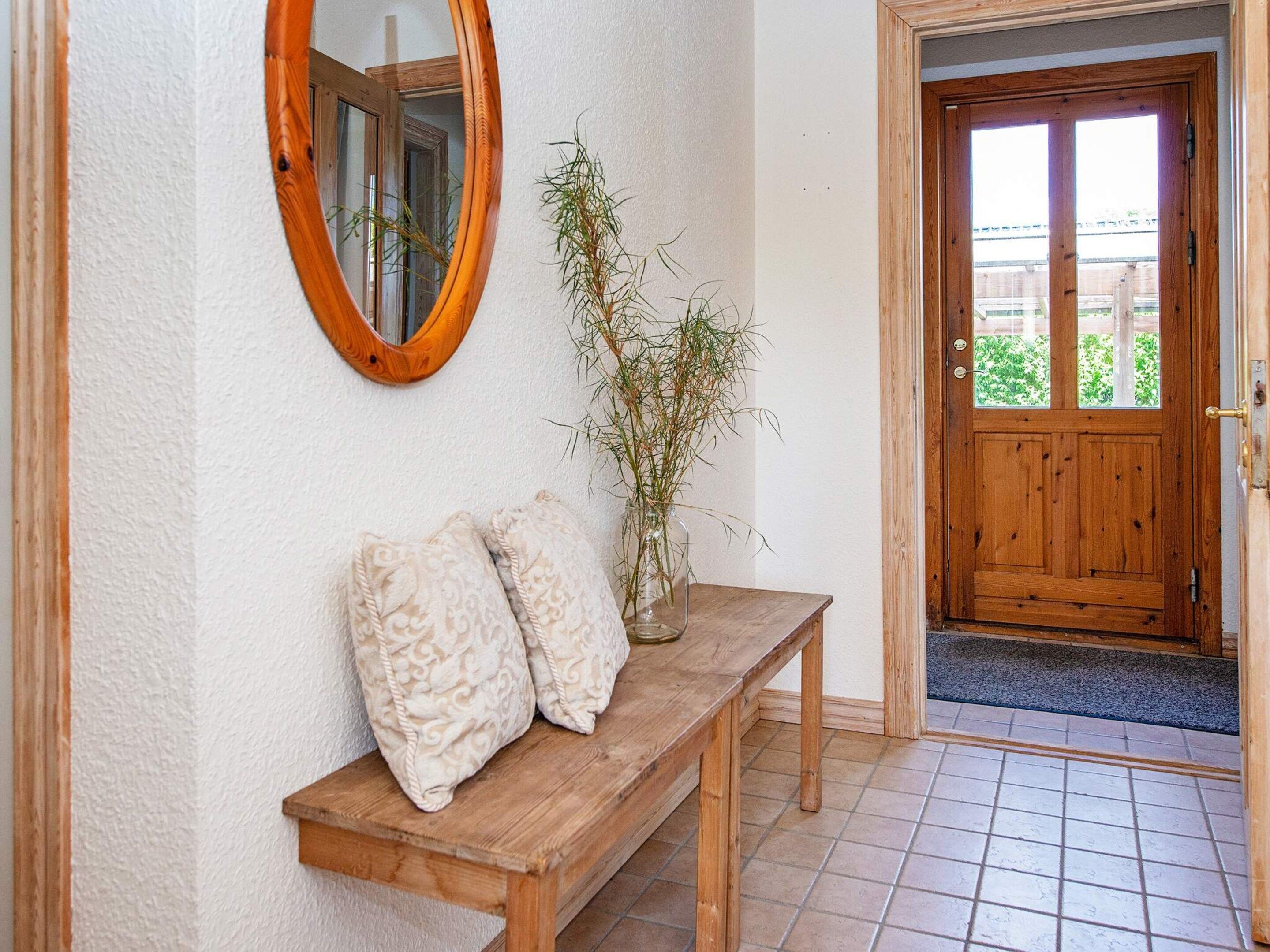 Um banco de madeira com almofadas, um espelho e uma planta de bambu em um corredor.