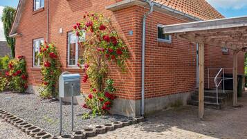 Uma casa de tijolos vermelhos com varanda coberta, caixa de correio e jardim com flores vermelhas.