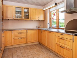 Cozinha com armários de madeira, pia de aço inoxidável e janela com vista para área verde.