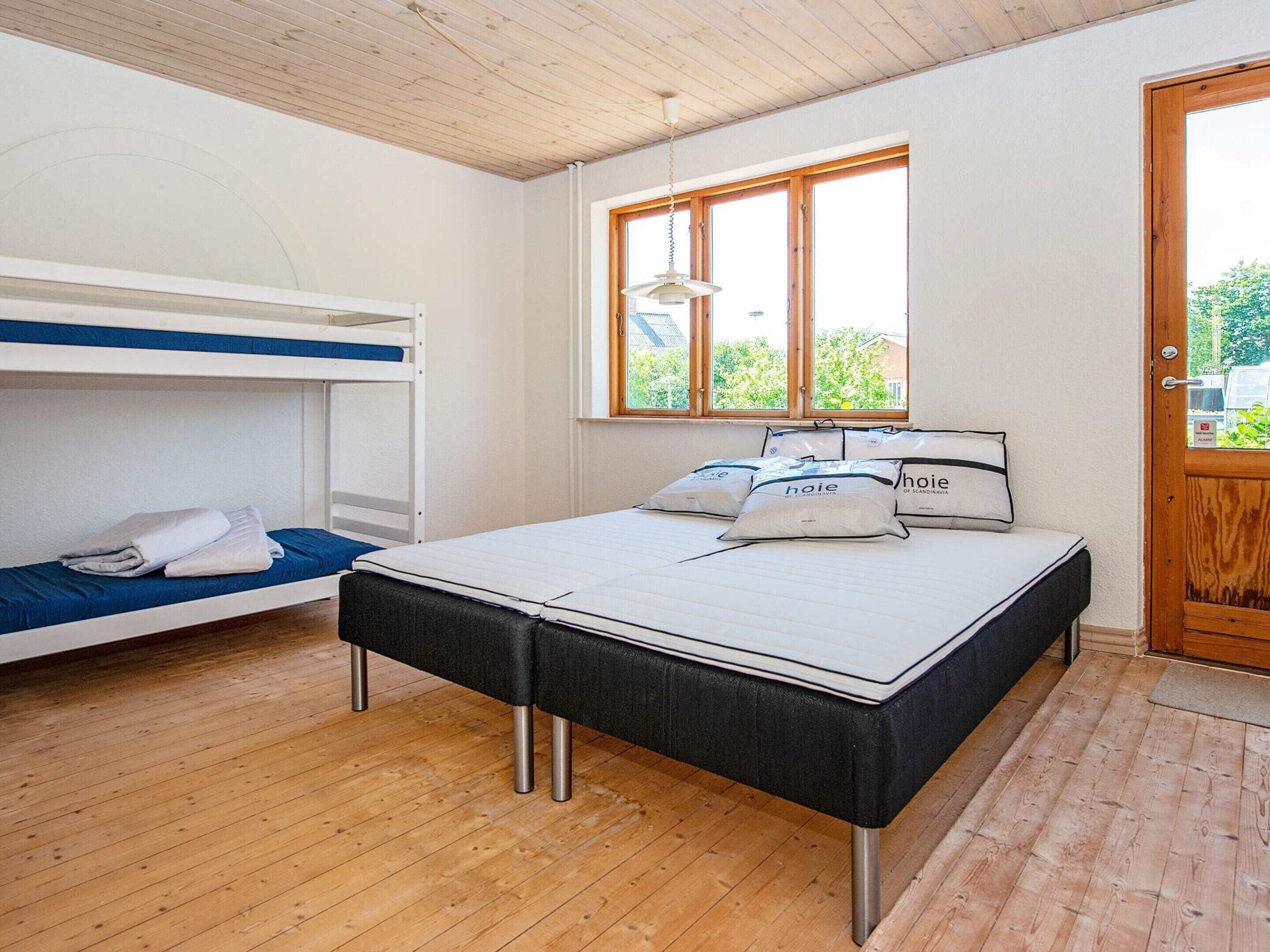 Quarto com beliche, uma cama de solteiro com travesseiros, janela com vista e porta de madeira.