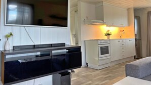 Uma cozinha moderna com armários brancos, forno embutido e fogão. Há uma televisão de tela plana fixada acima do balcão.
